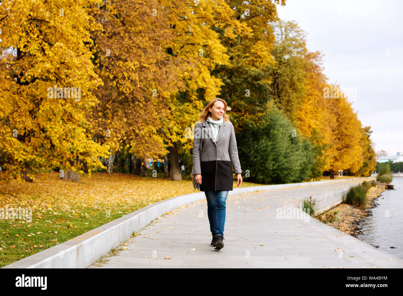 Elegant confident woman walking along the river in city park and ...