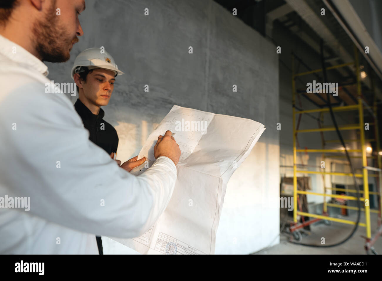 Two building engineers with blueprint working on construction site ...