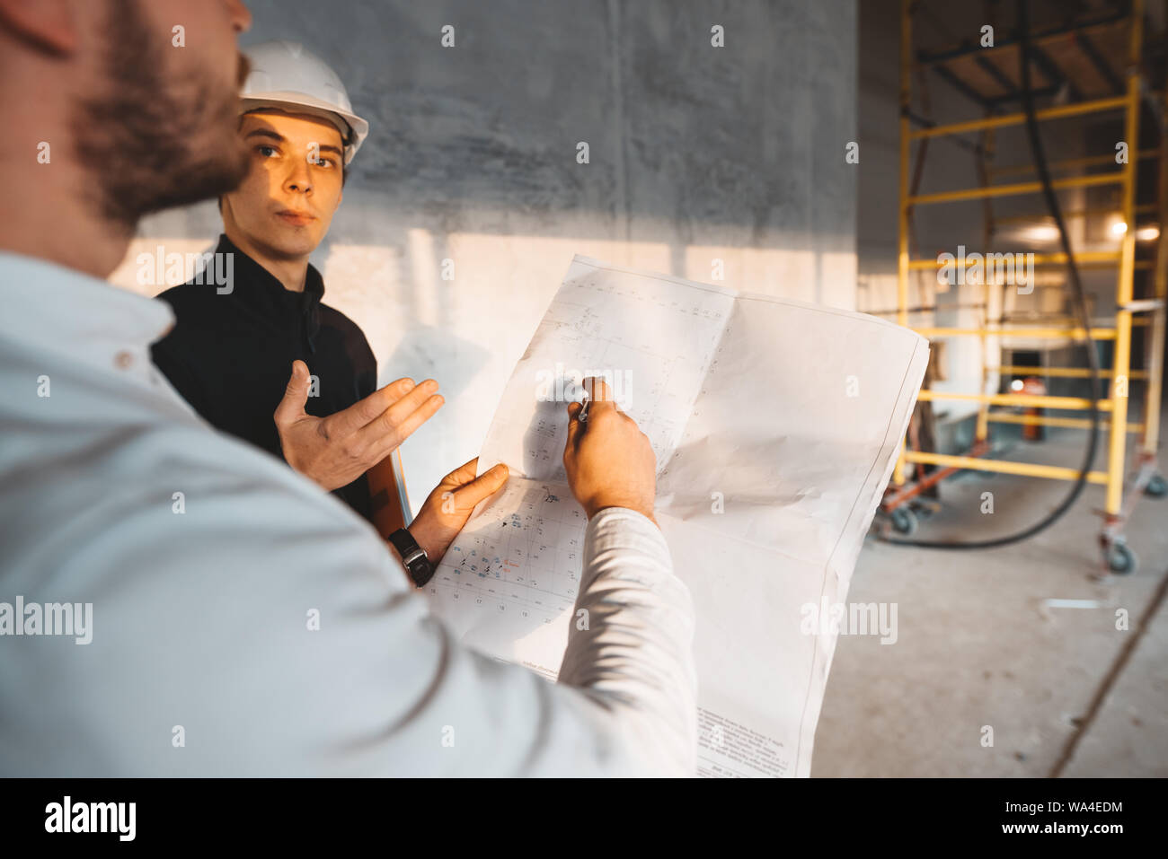 Building engineer and worker hold blueprint in hand while discussong ...