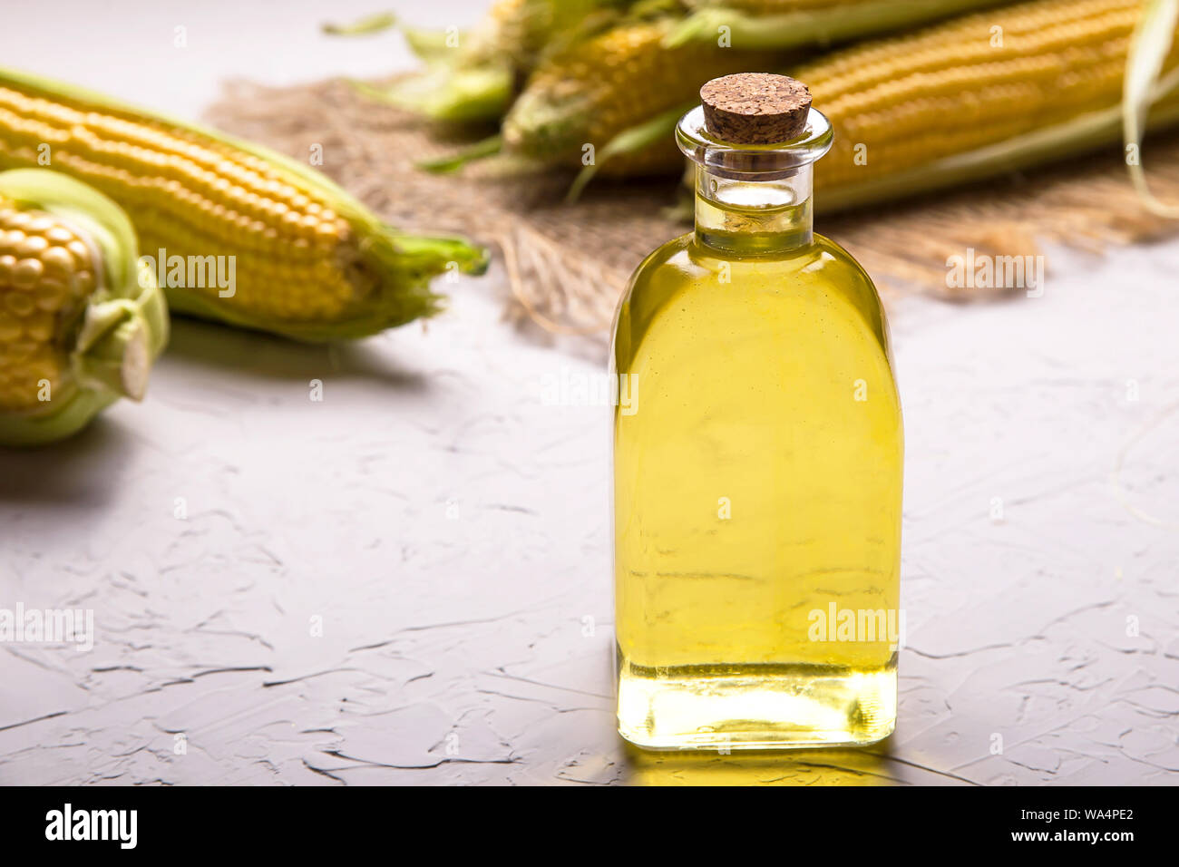 Glass bottle of corn oil with cork on a gray table with raw corn swings ...