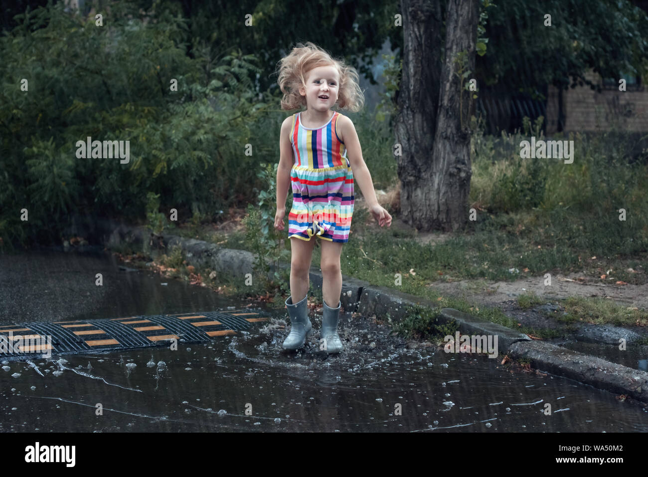 Cute baby girl jumping in the rain through the puddles Stock Photo - Alamy