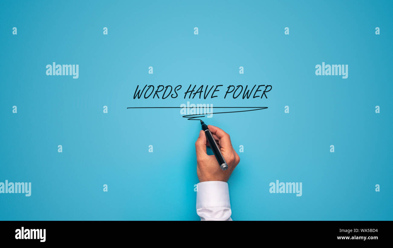 Male hand writing a Words have power sign with black marker on blue ...