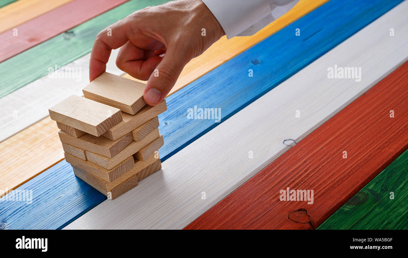 Hand of a businessman building a stack of wooden pegs over colorful ...