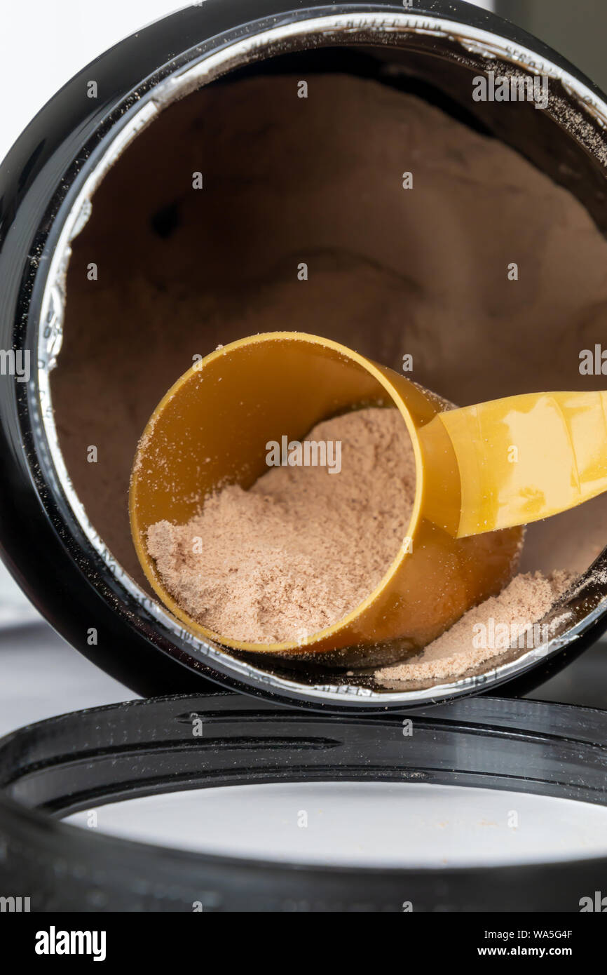 Plastic measuring spoon and heap of brown chocolate protein powder ...