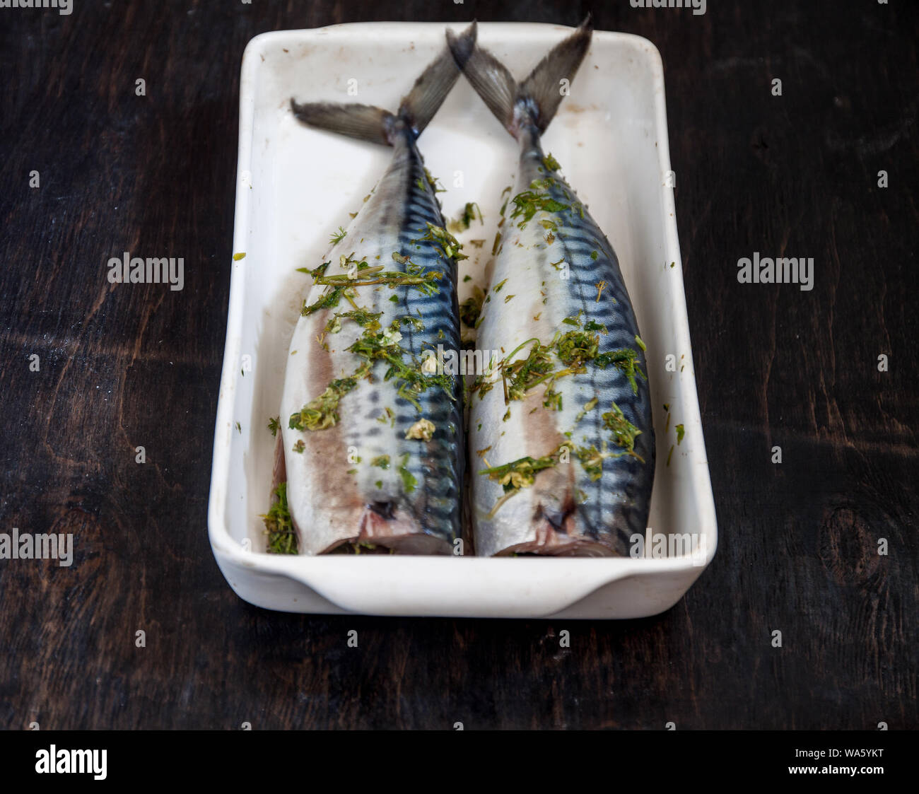 two raw fish mackerel in greens and herbs will be baked on a dark ...