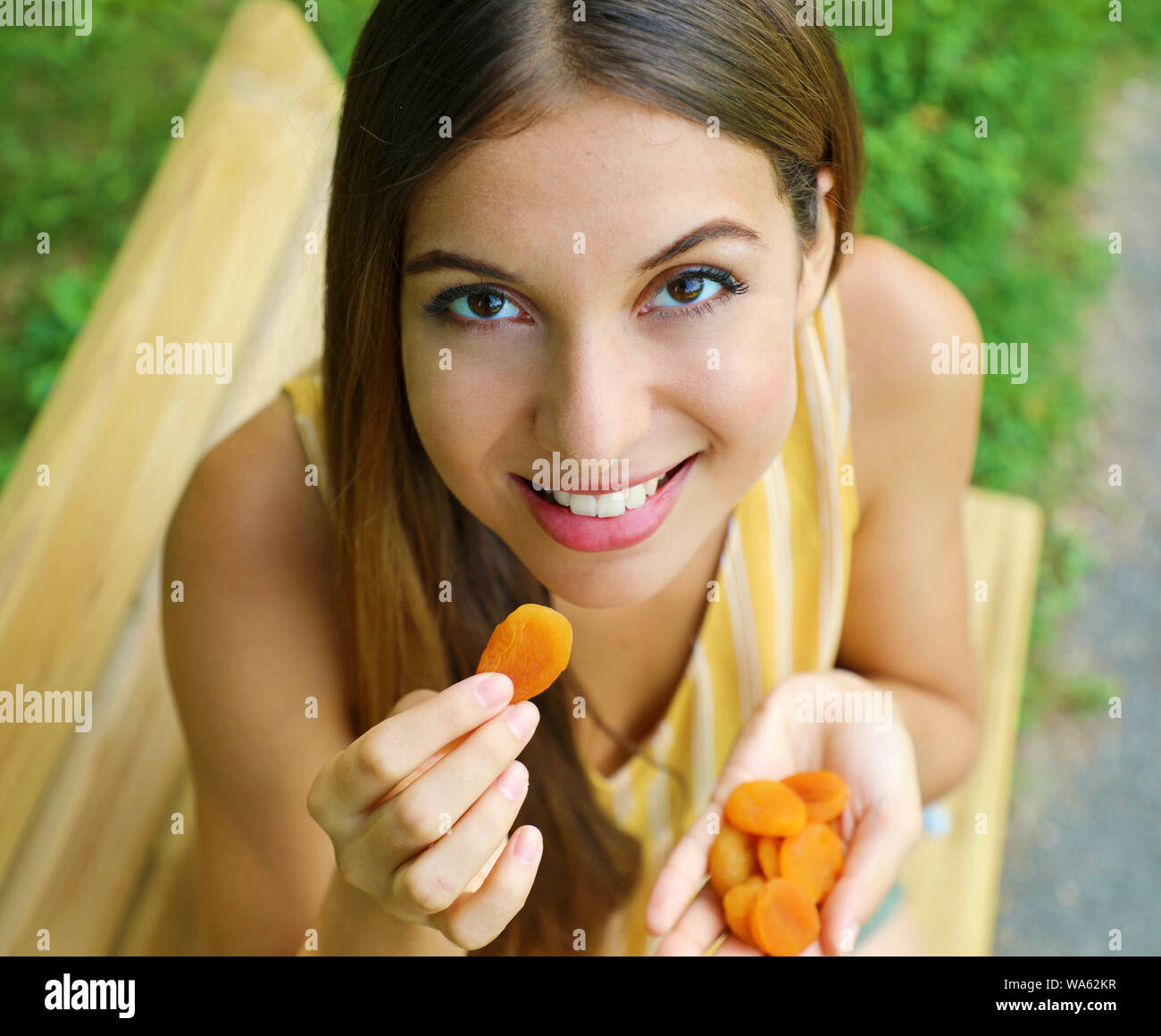 Young woman eating dried apricots in the park. Healthy food concept ...