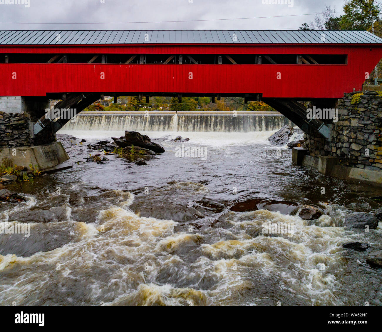 A red covered bridge first built in 1883 spans a rapidly flowing river ...