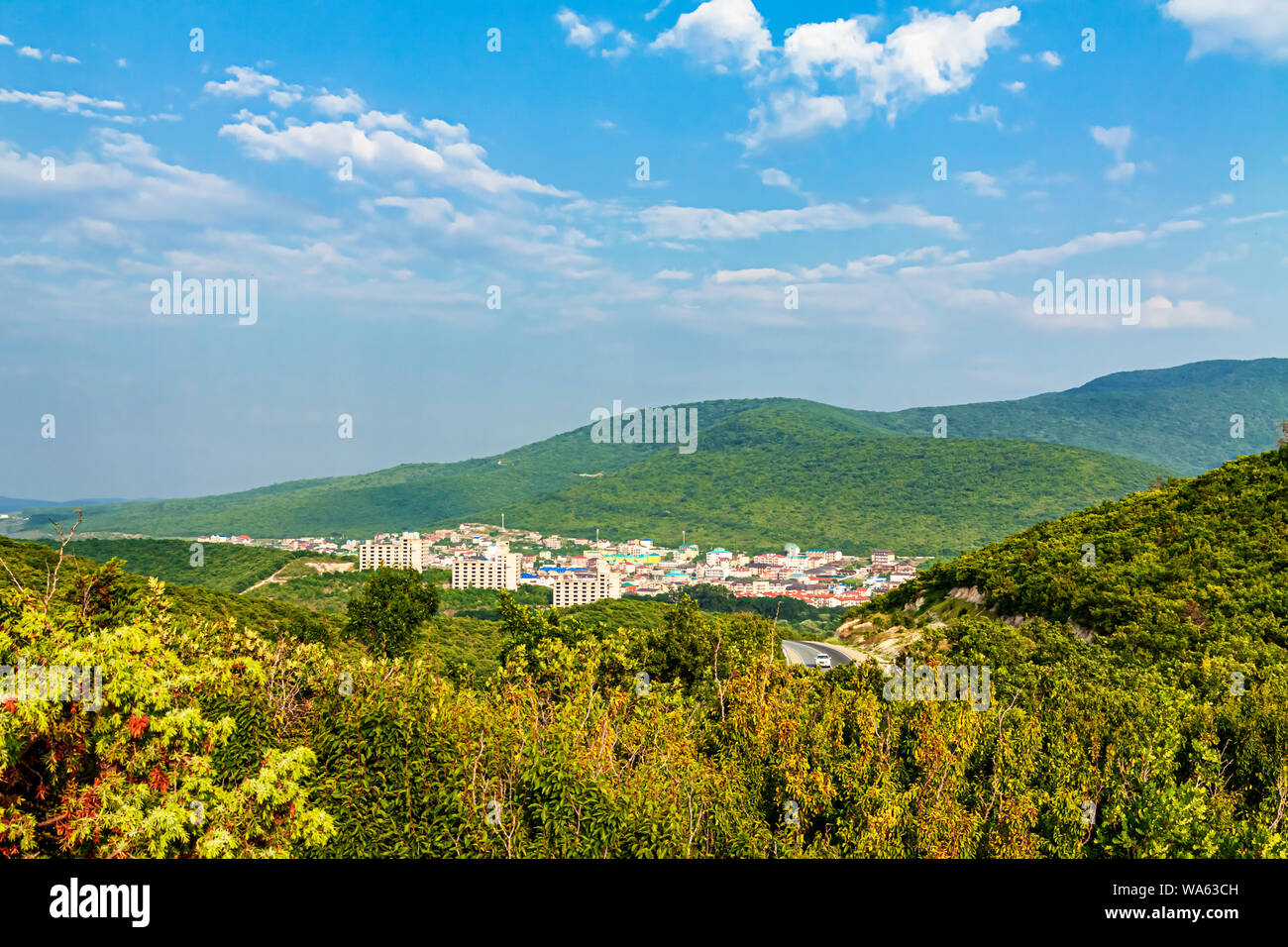 A small town among small mountains, forests against a blue sky with ...