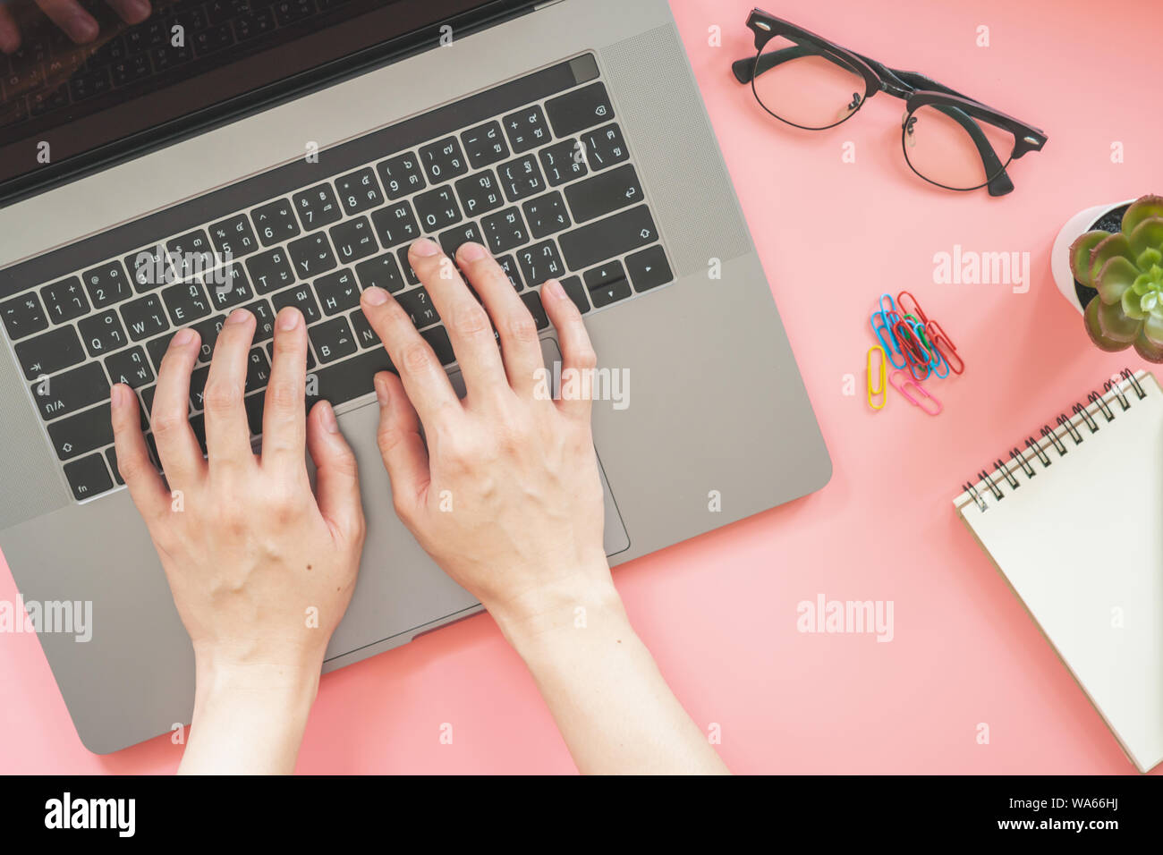 woman typing on laptop in pink pastel colourful office with accessories ...