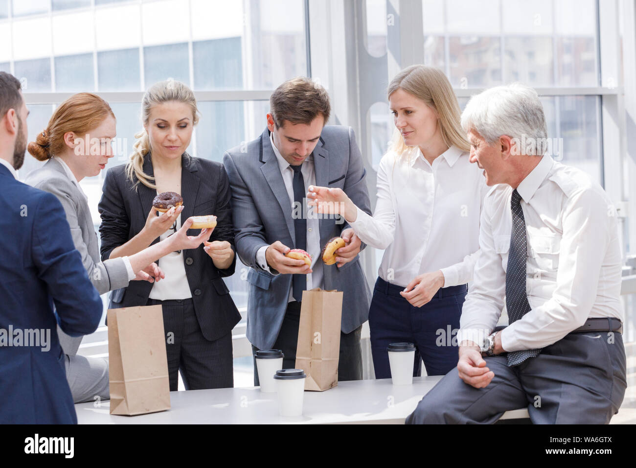Business people having coffee break eating donuts together in office ...