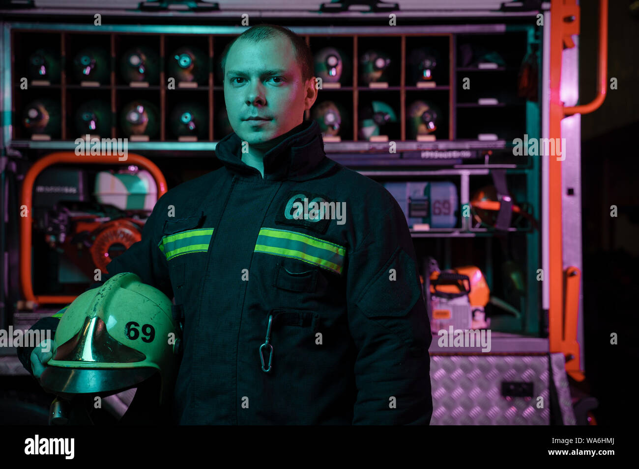 Portrait of serious fireman looking to camera in fire uniform near fire ...