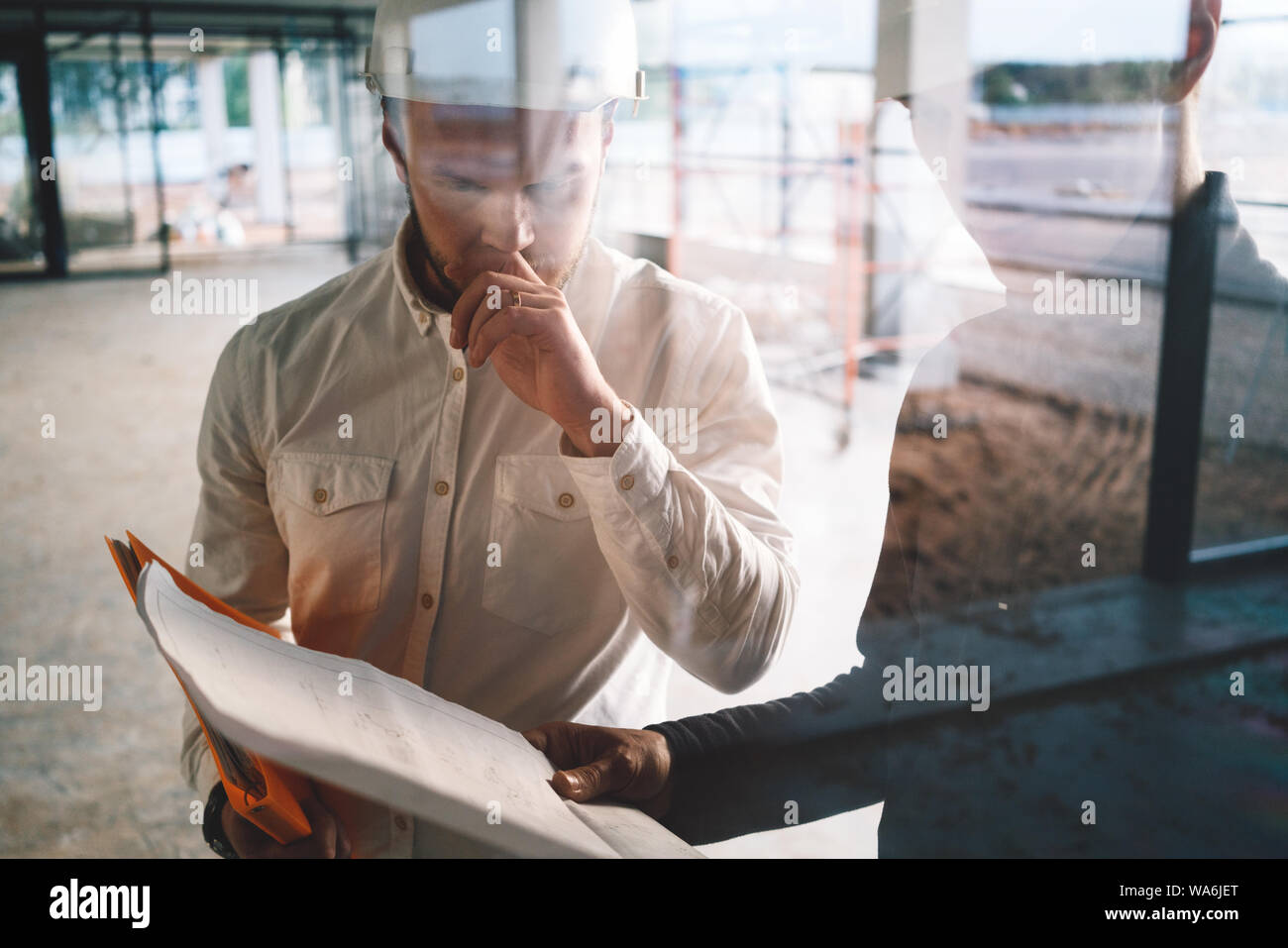 Two building engineers wearing safety hard hat discussing blueprint on ...