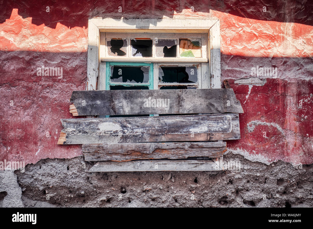 Window with broken glass and barred shut with planks on red wall of an ...