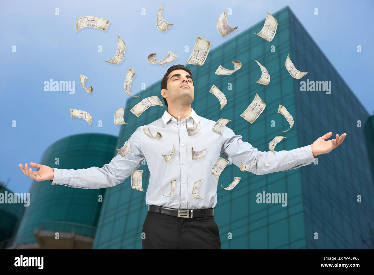Money falling on a businessman standing with his arms outstretched ...