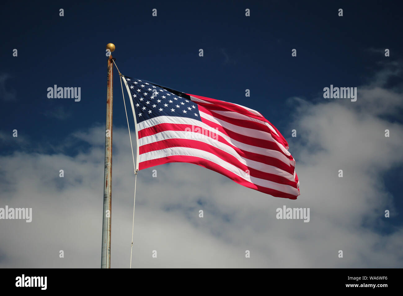 american flag on a pole wavering against a vibrant blue sky with white ...