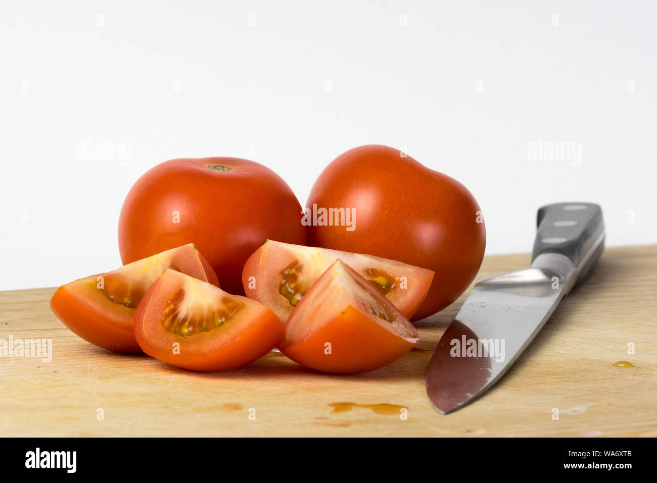 Three red tomatoes, one cut into quarters, on chopping board with knife ...