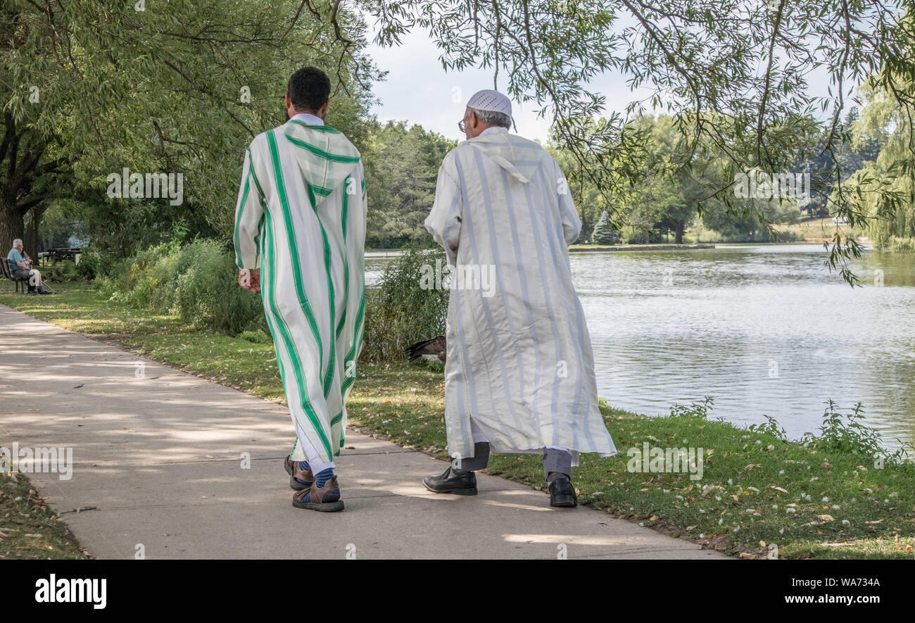 Two muslim men, traditionally dressed, walking thru the park. Viewed ...