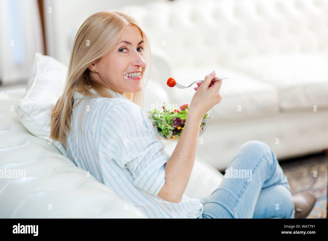 Mature woman eating a healthy salad on her sofa Stock Photo - Alamy