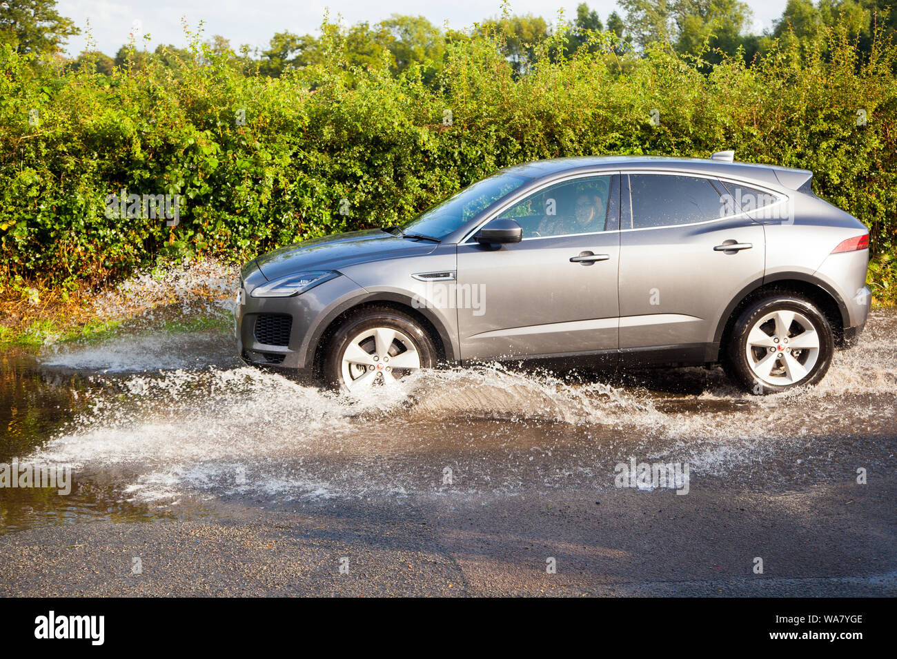 Car driving through water along a flooded country road / lane during ...