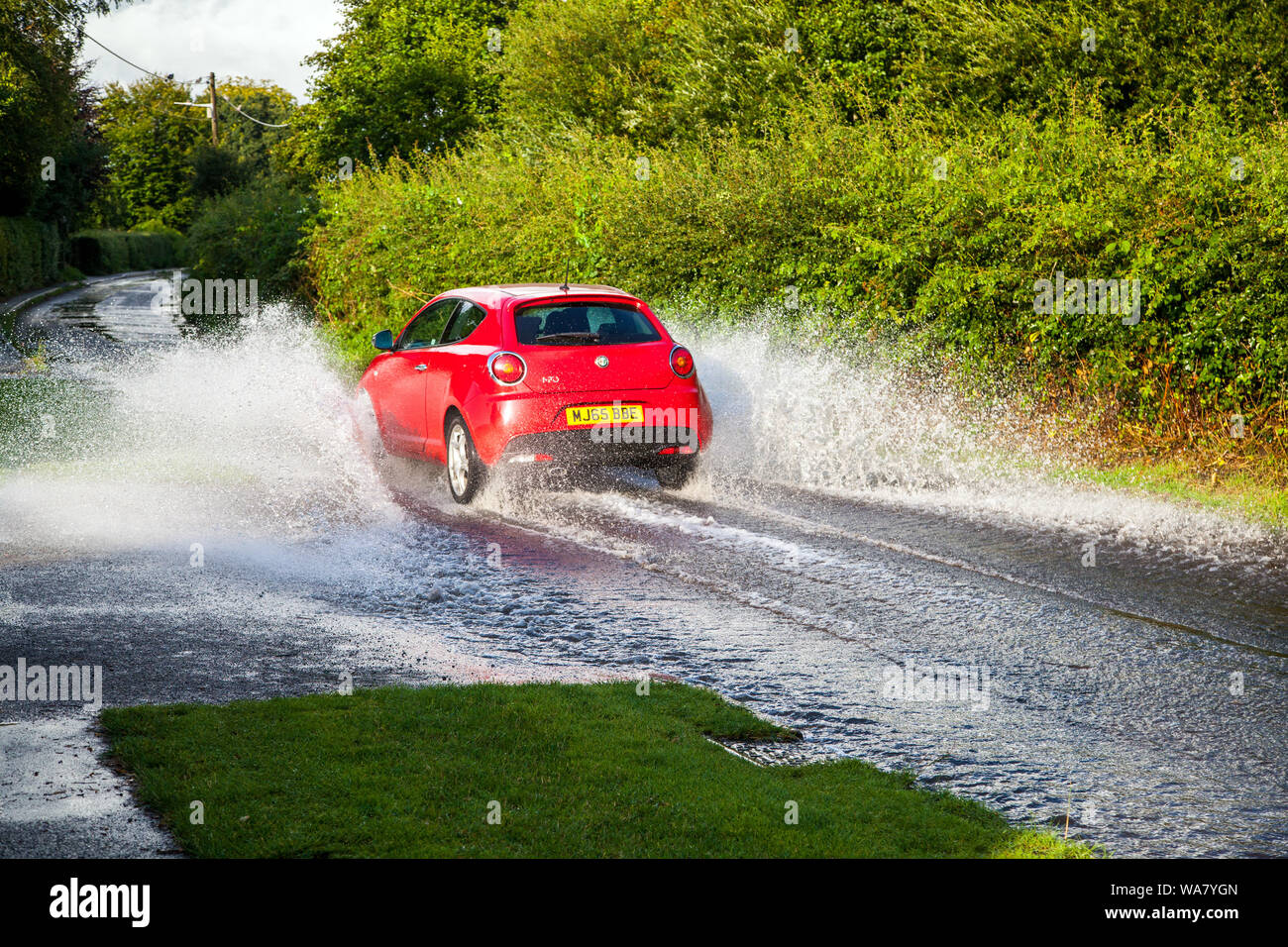 Car driving through water along a flooded country road / lane during ...
