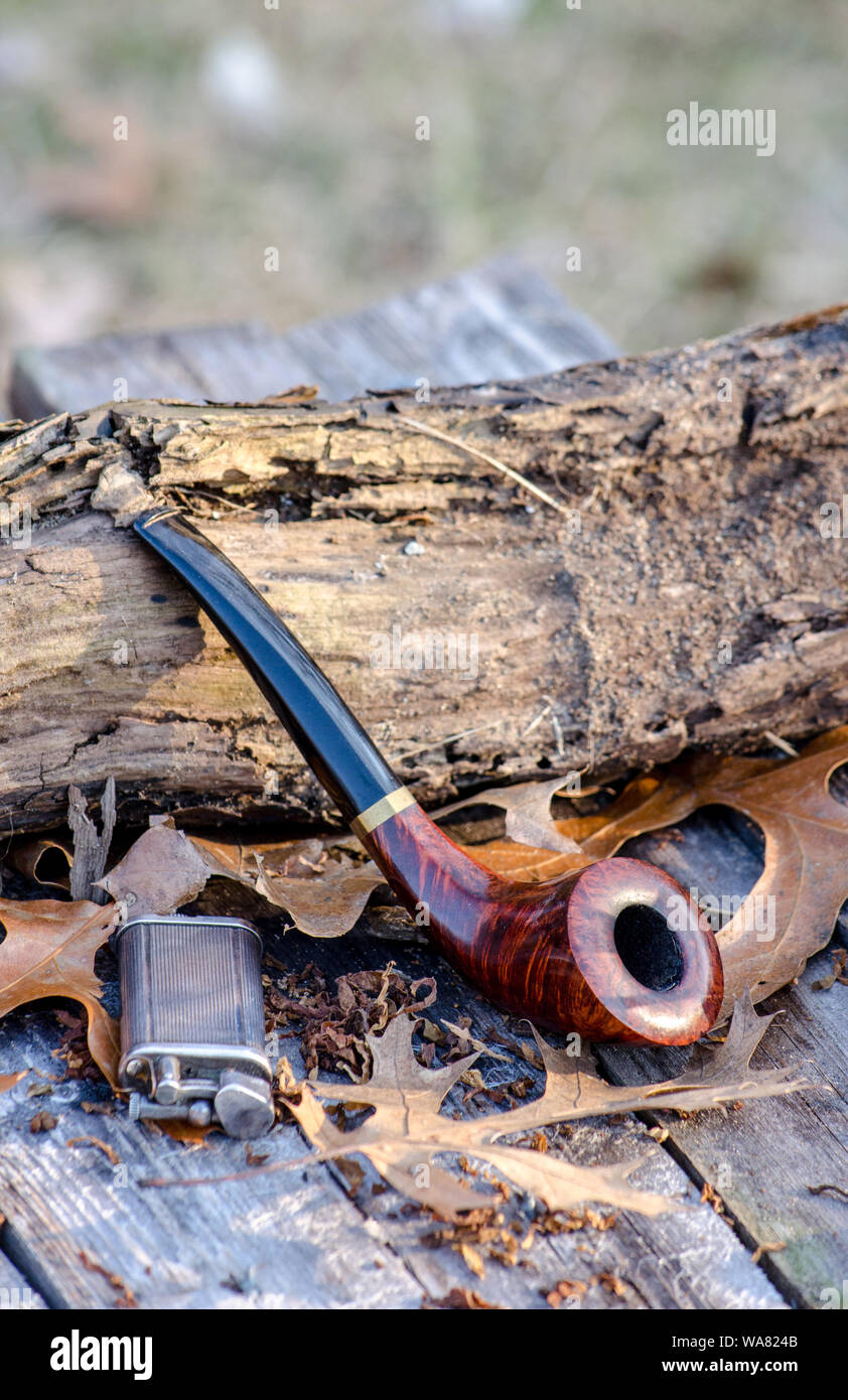 Brier horn shaped pipe with lighter on a rustic outdoor background ...