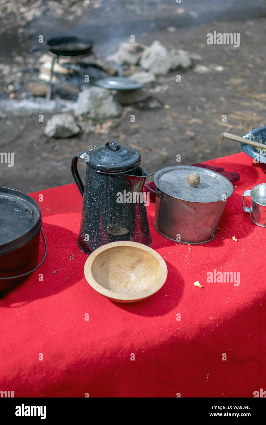 a smoking camp fire and utensils for outdoor cooking, are set up at an ...