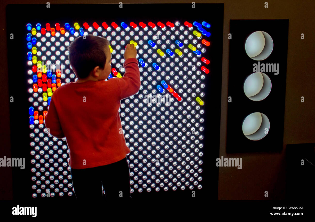 child creating patterns on a giant lit grid with transparent pegs that ...