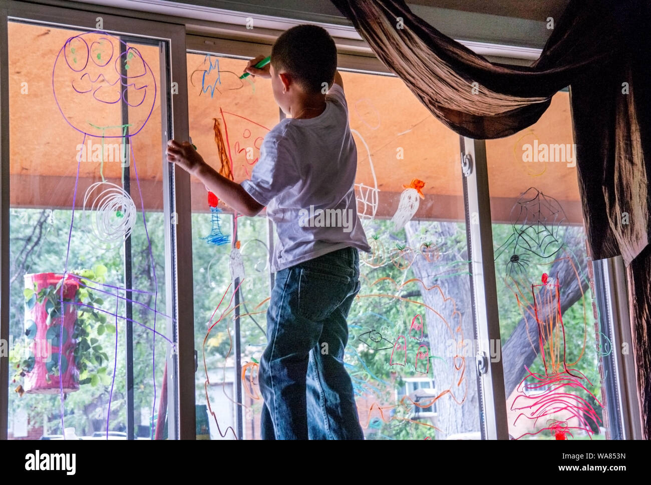 child decorates a window for Halloween, with colorful window markers ...