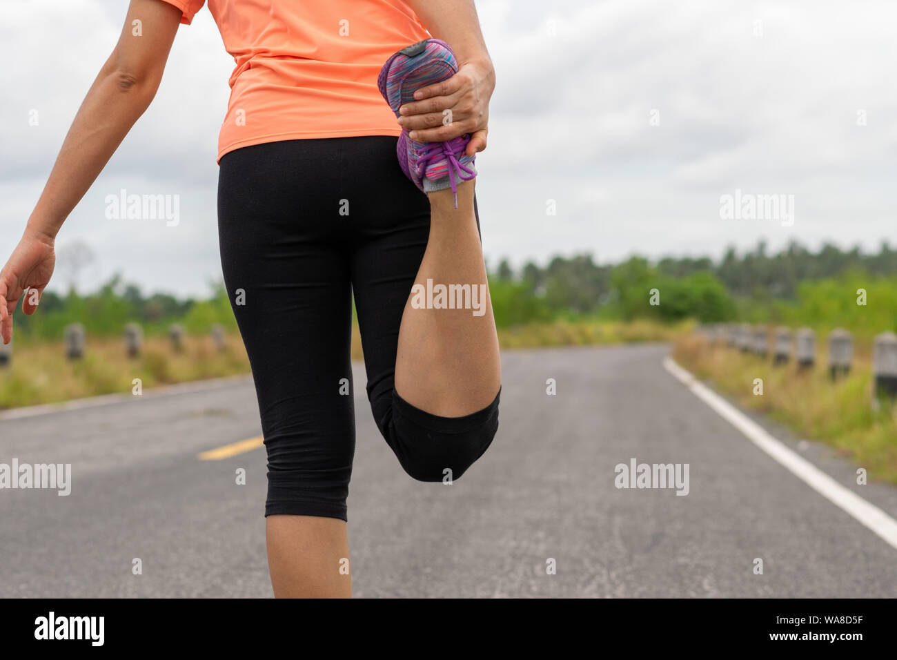 Young fitness woman runner stretching legs before run in the park. Outdoor exercise activities ...