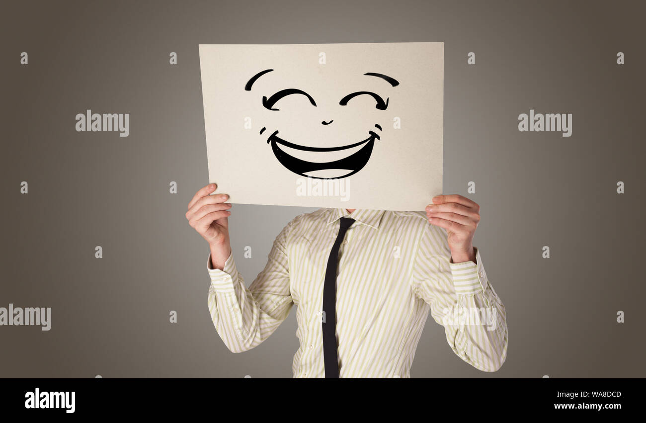 Casual person holding a paper in front of his face with drawn emoticon ...
