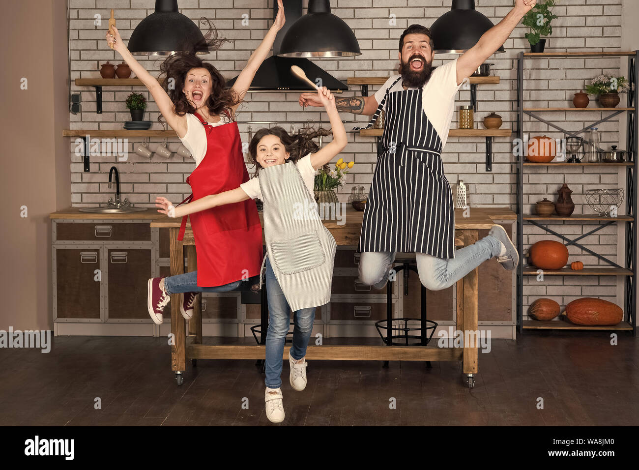 Having fun in kitchen. Family mom dad and little daughter wear aprons ...