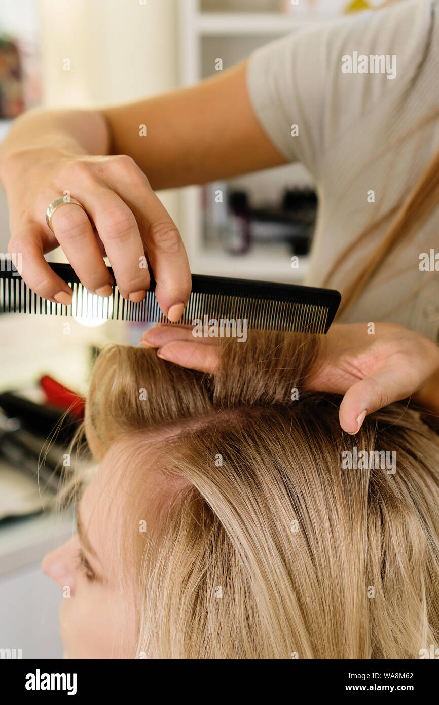 Female hairdresser making hairstyle to blonde girl in beauty salon ...