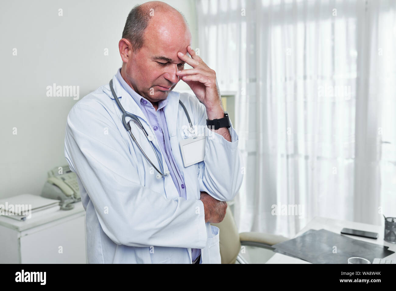 Stressed doctor standing in his office and thinking about difficult ...