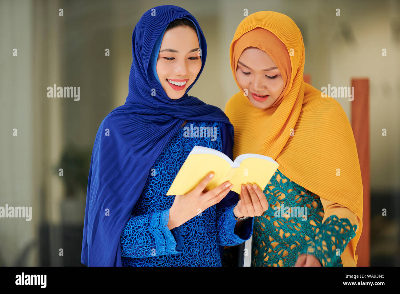 Smiling pretty young Vietnamese muslim women reading holy book together ...