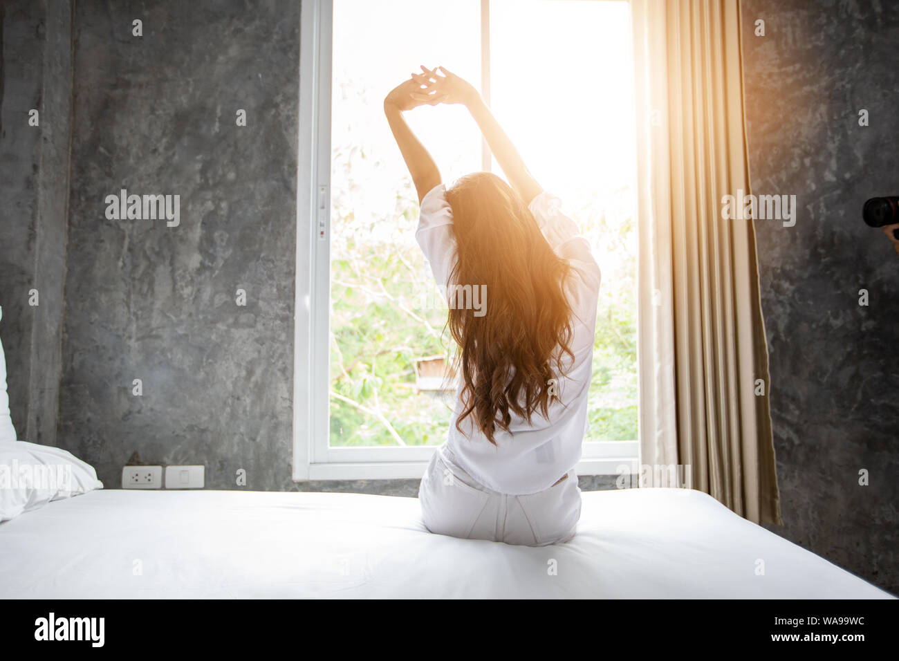 Asian woman waking up in her bed fully rested and open the curtains in ...