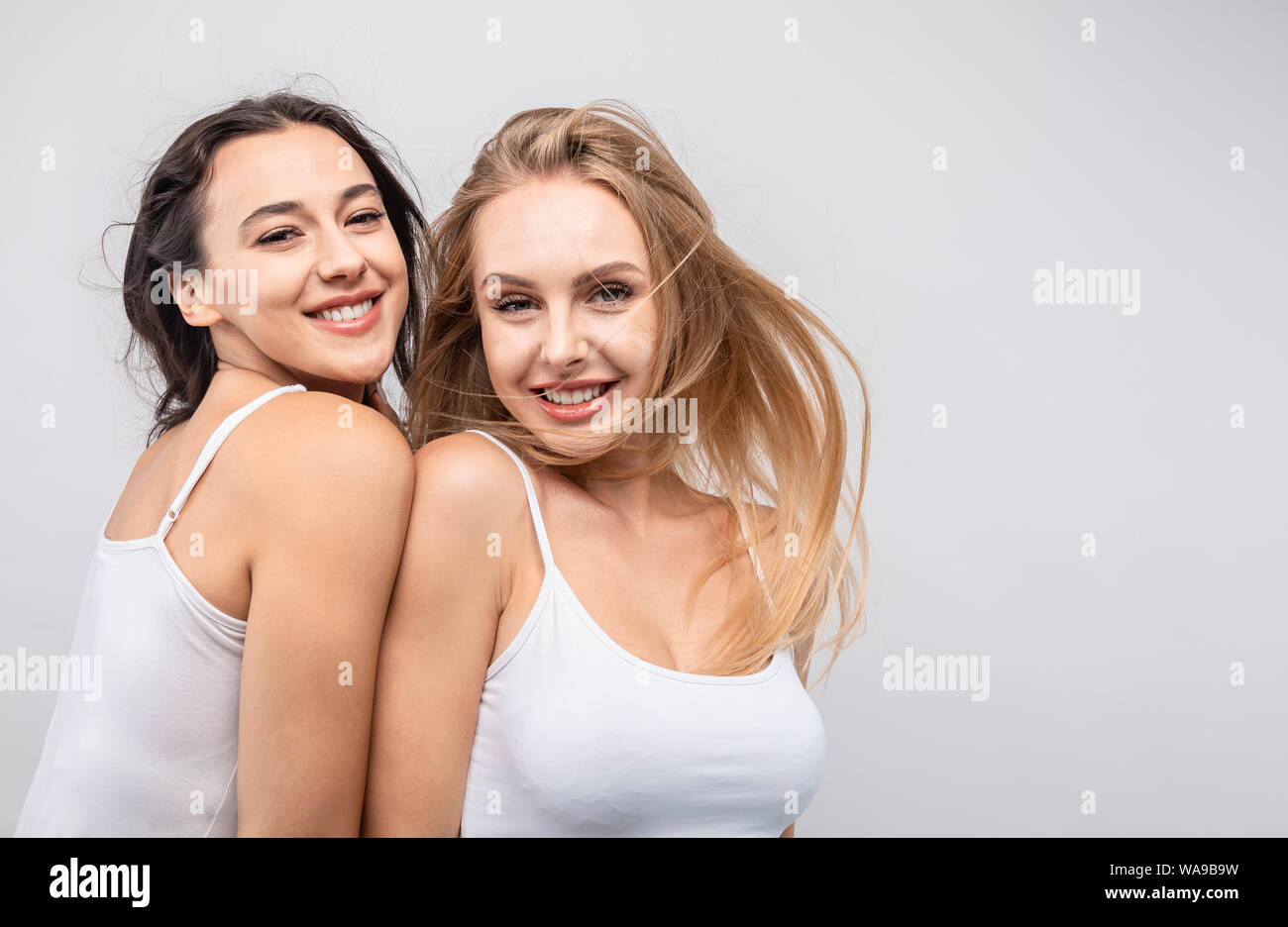Smiling girls in white tank tops nestling each other looking at camera ...