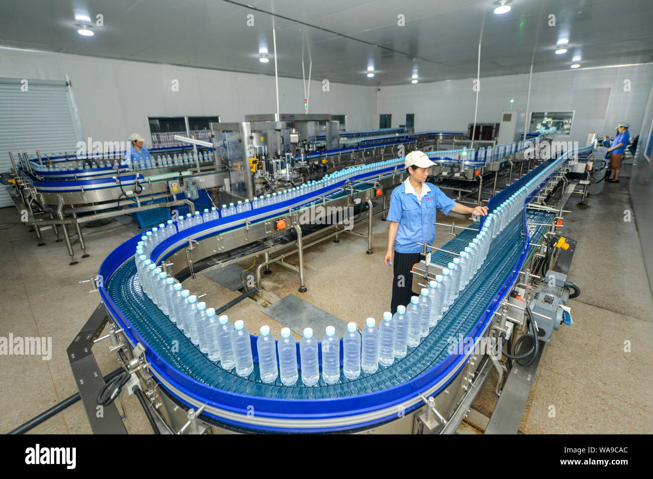 Chinese workers produce bottles of mineral water on an assembly line at ...