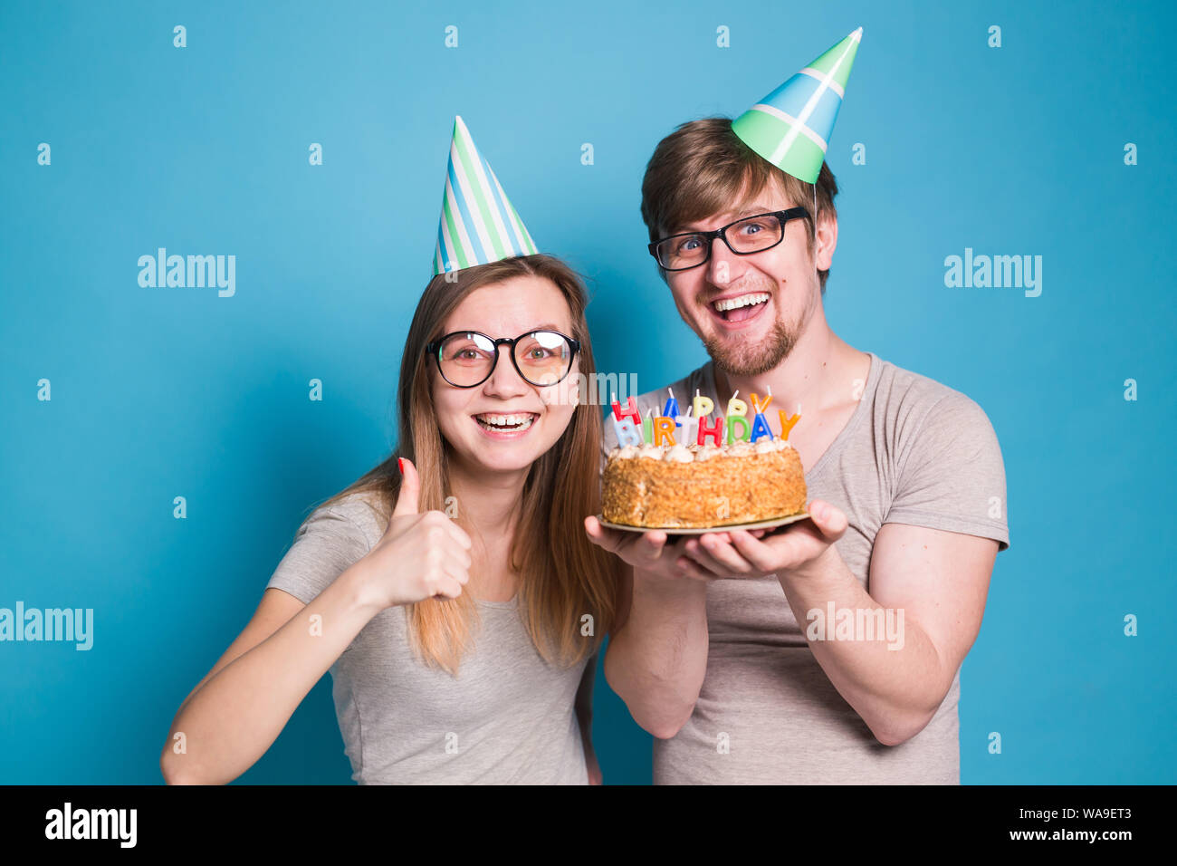 Funny young couple in paper caps and with a cake make a foolish face ...