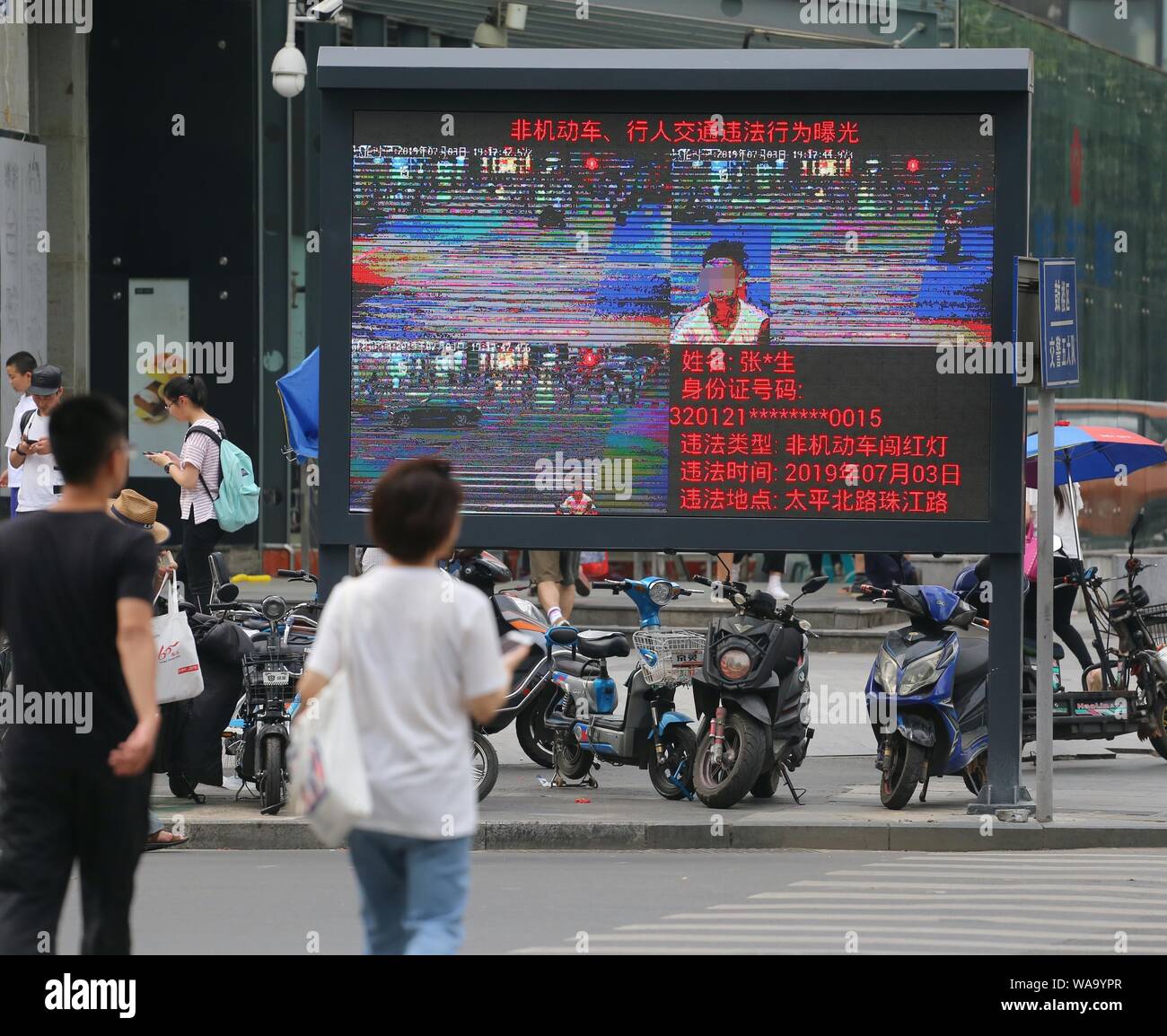Pedestrians walk across a crossroad as a big electronic screen ...