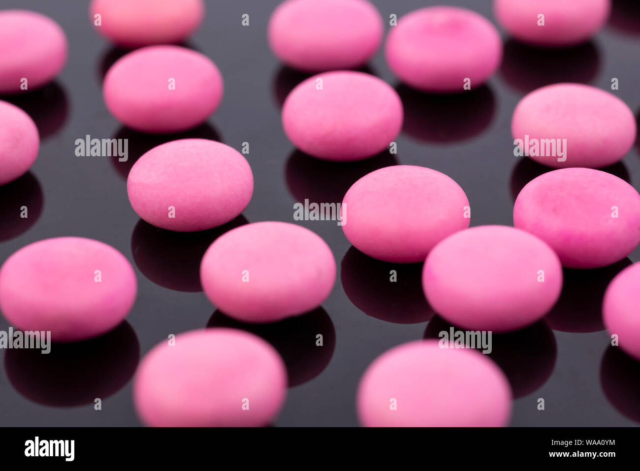 Pink pills isolated on black reflective surface. Global pharmaceutical ...