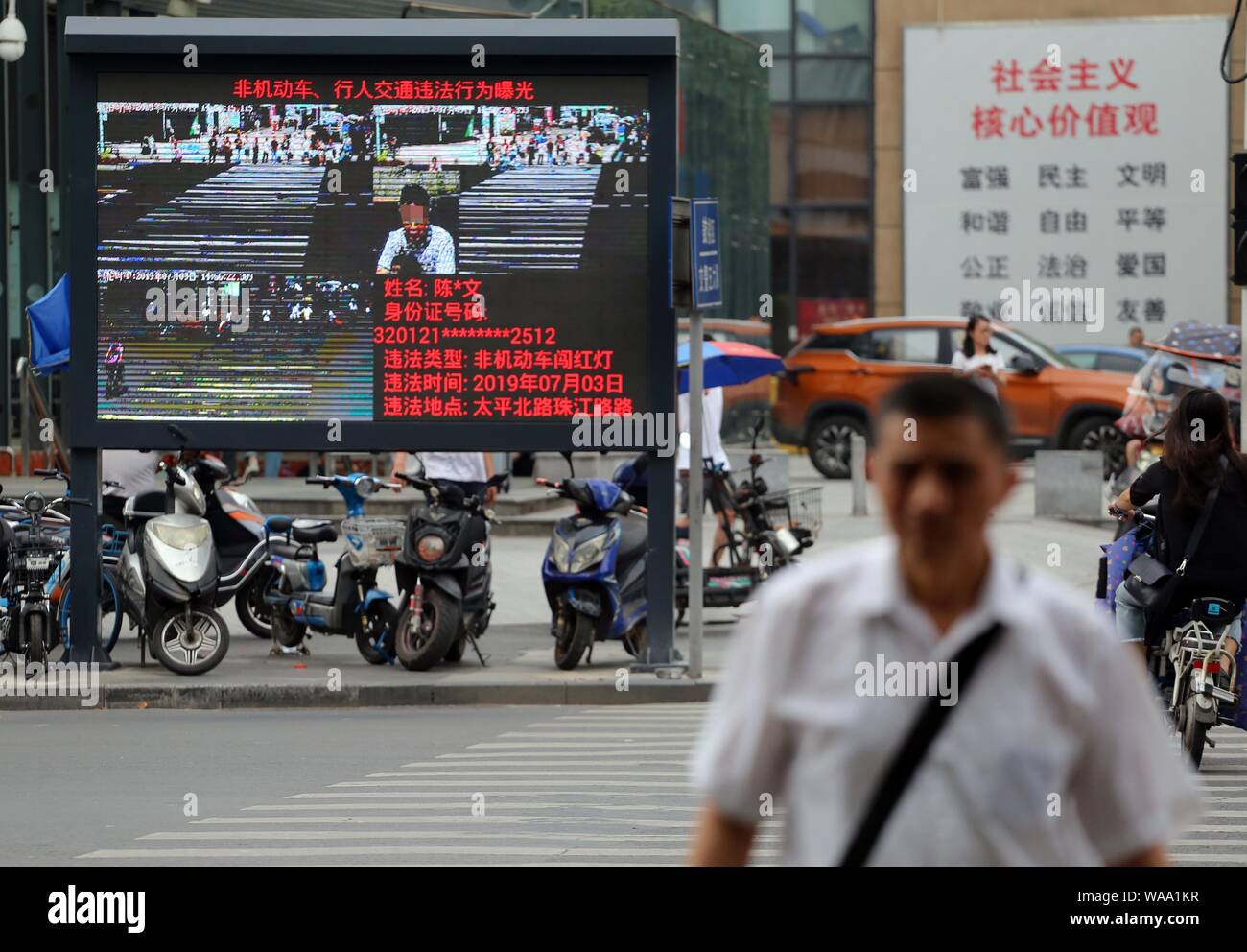 Pedestrians walk across a crossroad as a big electronic screen ...