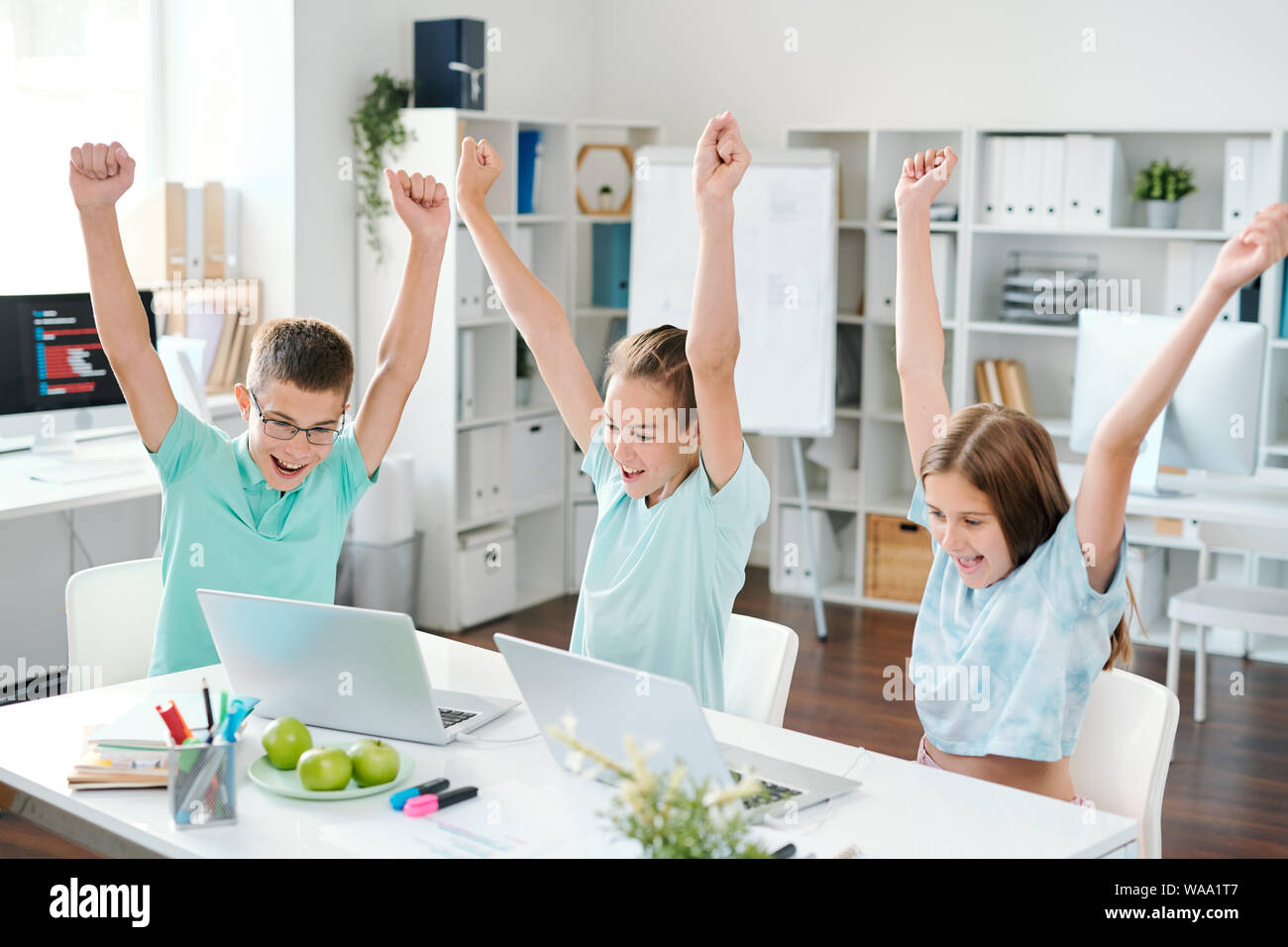 Cheerful middle school students with raised hands looking at laptop ...
