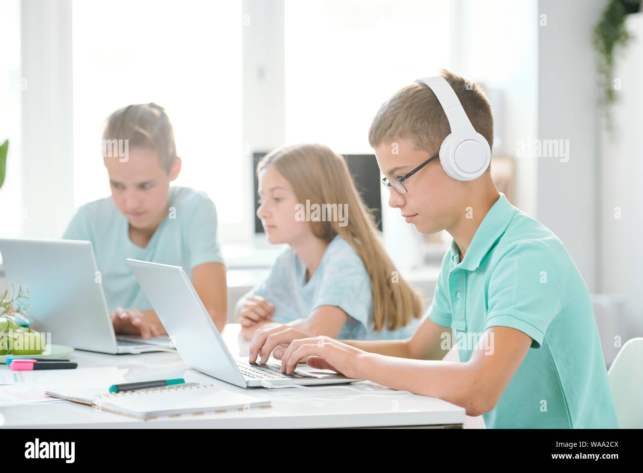 One of youthful classmates in headphones looking at laptop display ...