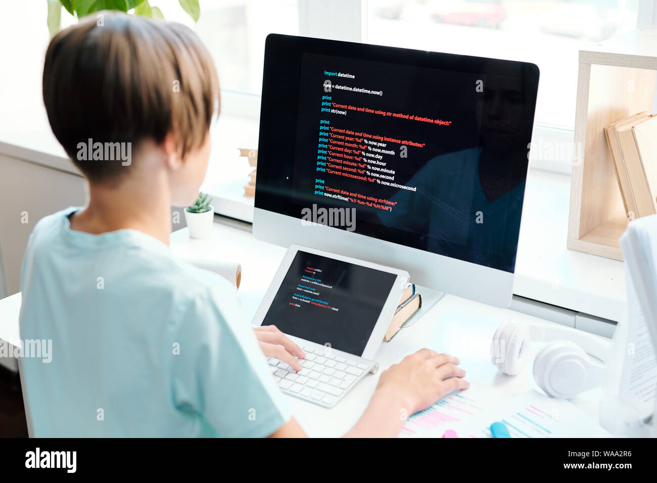 Contemporary schoolboy sitting by desk in front of computer monitor ...