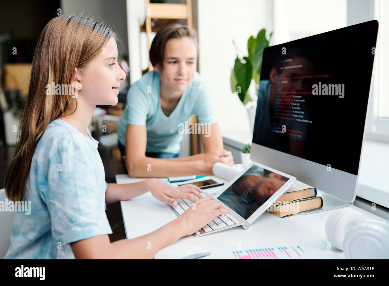 Pretty youthful girl typing on computer desktop keypad while looking at ...
