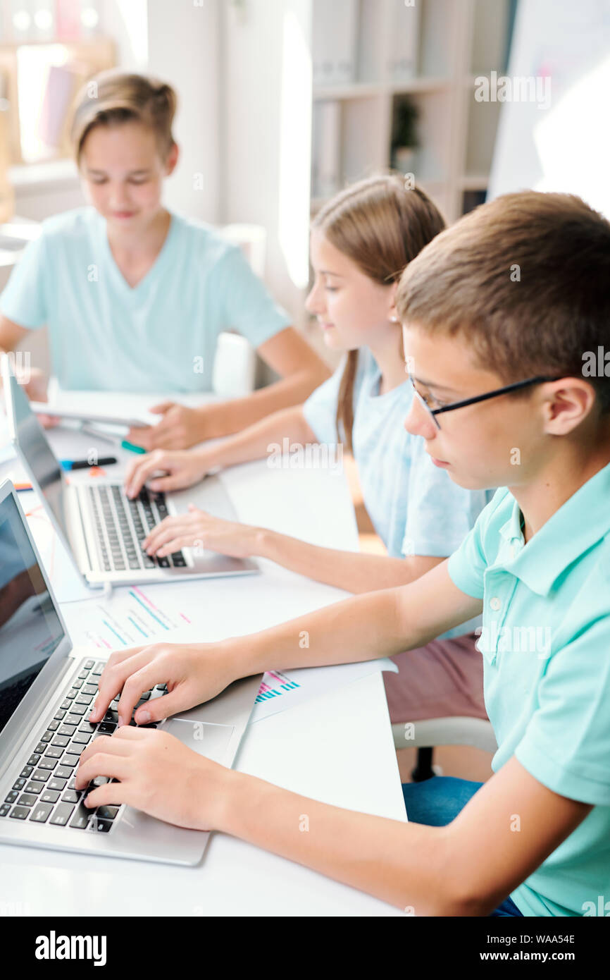 Two boys and girl sitting in front of laptops while carrying out final ...