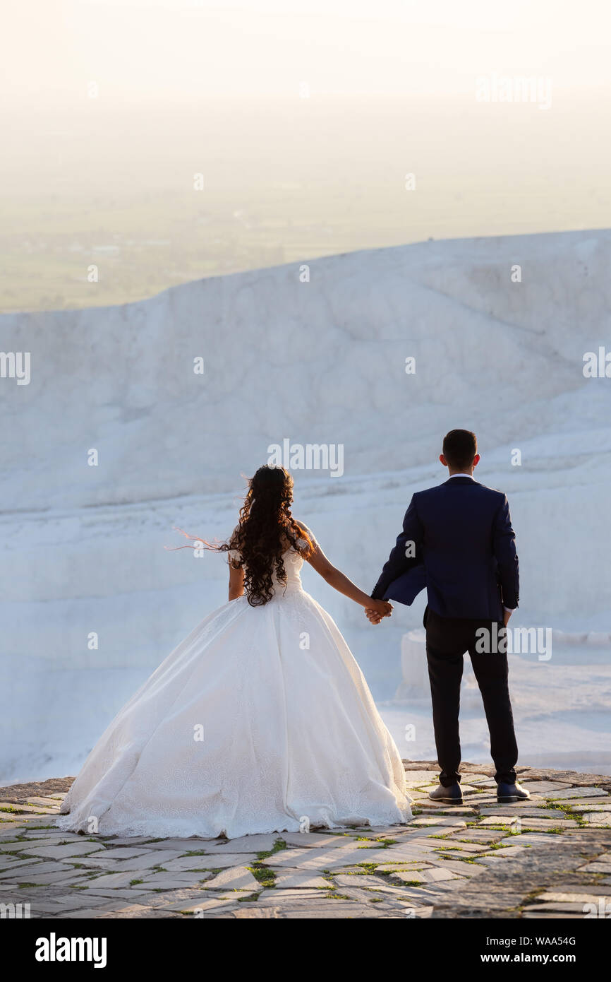 Young wedding couple stands over cliff holding hands and looks into the ...