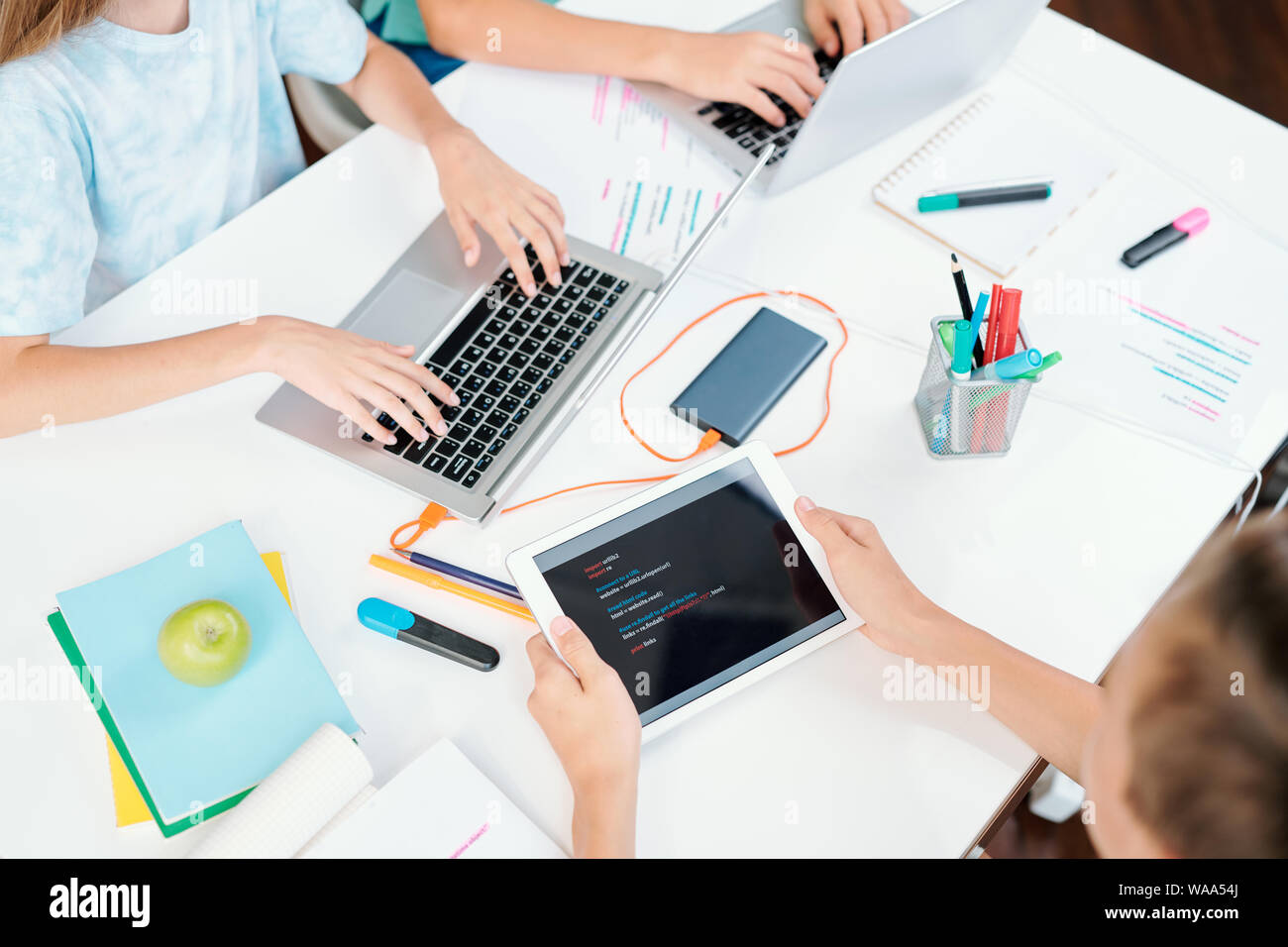 Hands of three clever school learners with modern mobile gadgets over ...
