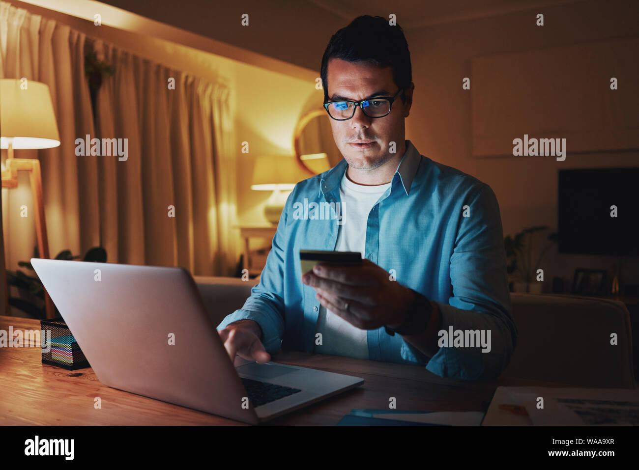 Man using credit card and laptop for paying bills online late at night ...