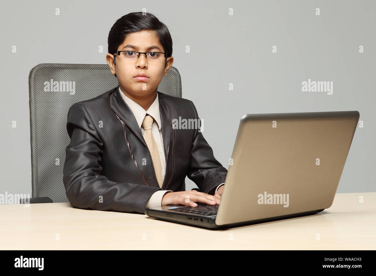 Boy pretending to be a businessman working on a laptop in an office ...